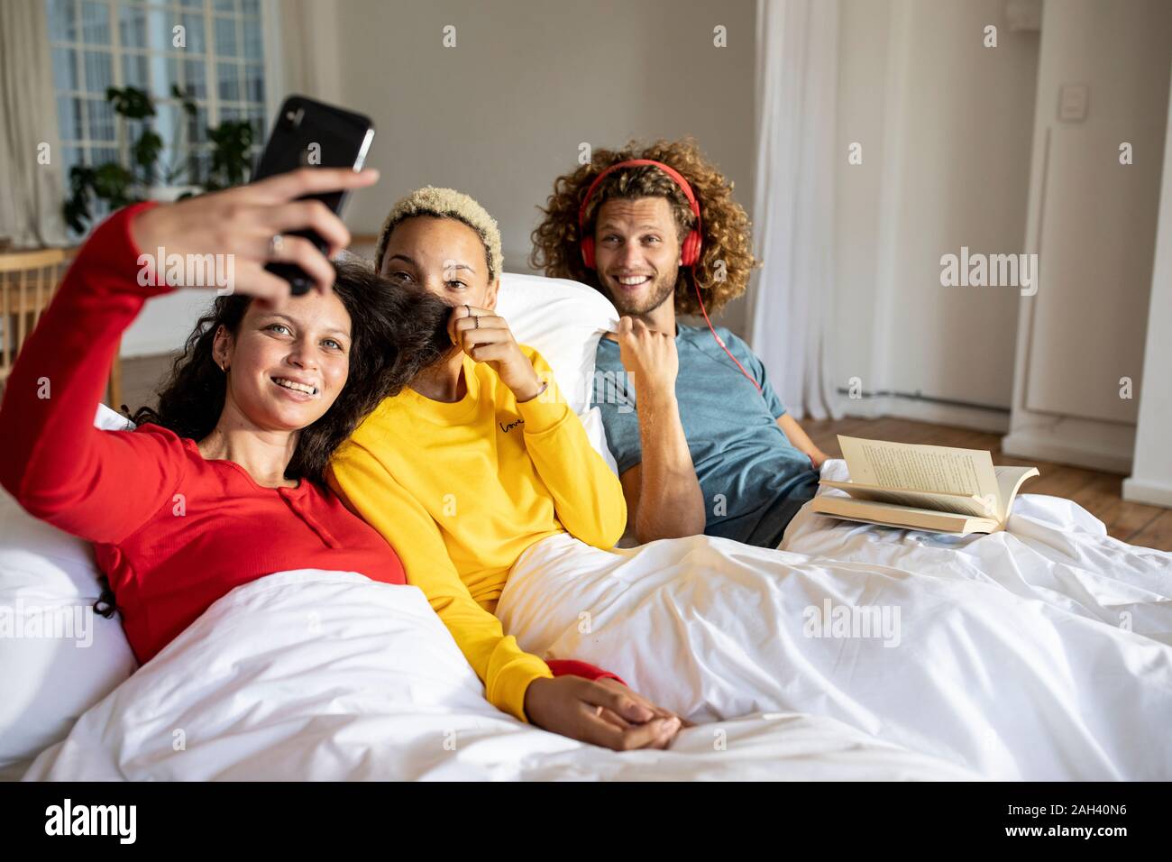 Happy friends relaxing in bed at home with smartphone Stock Photo - Alamy