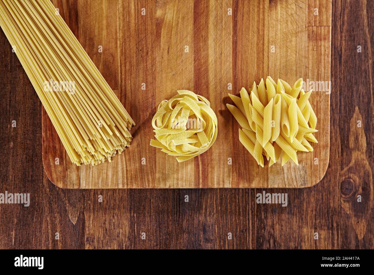 Various types of pasta on wooden table with cutting board, top view ...