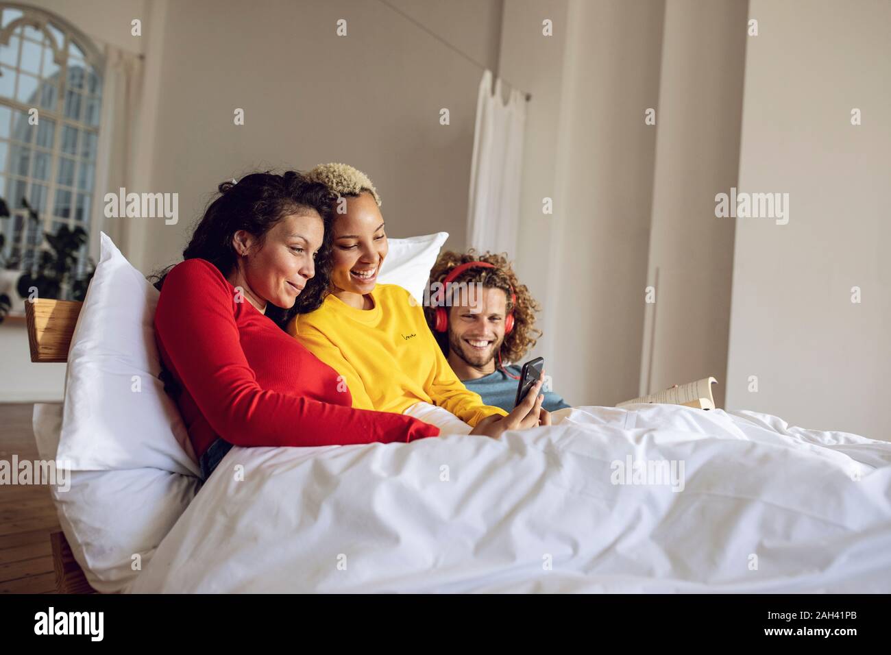 Happy friends relaxing in bed at home with smartphone Stock Photo - Alamy