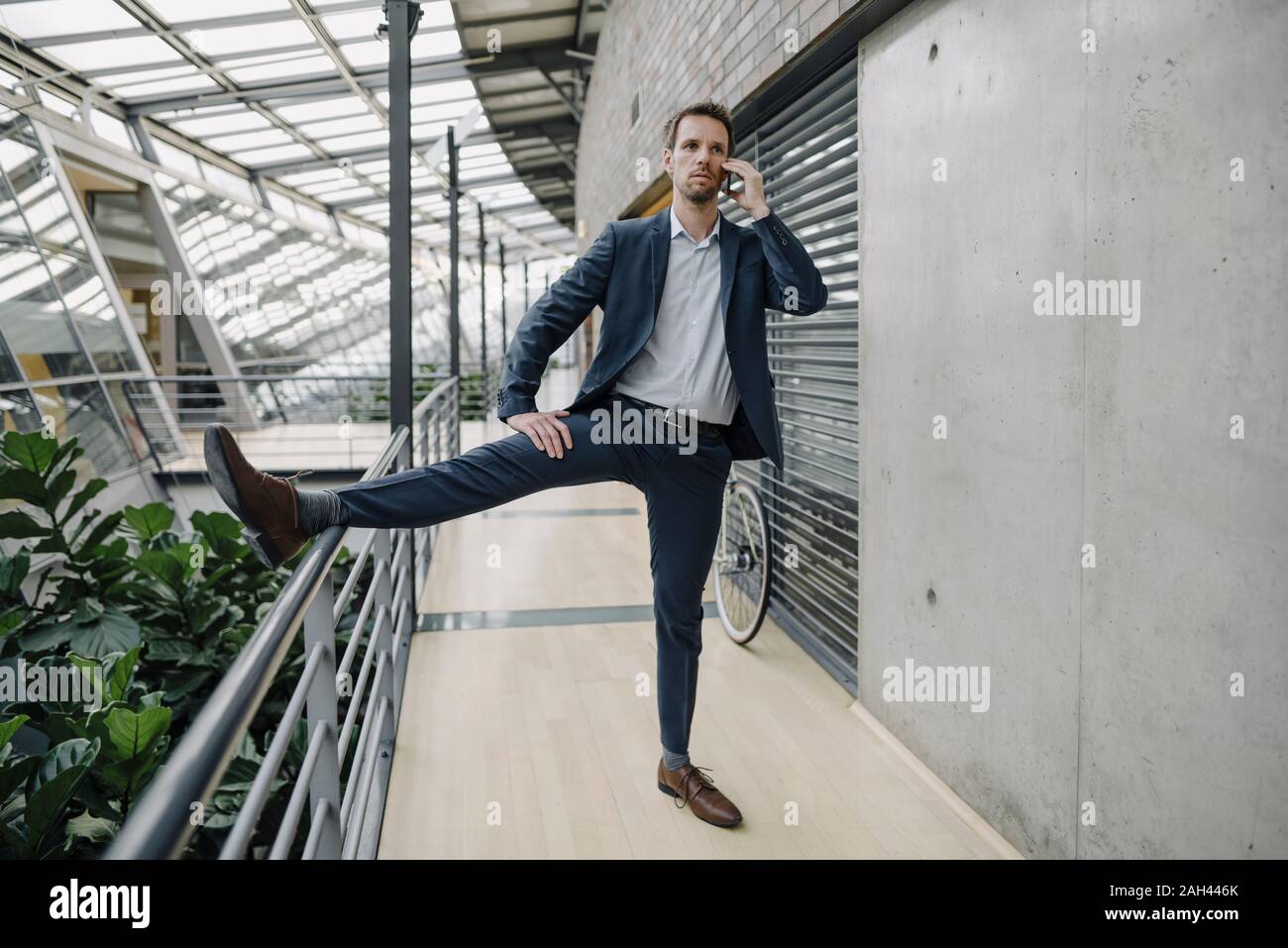 Businessman standing on one leg in modern office building talking on ...