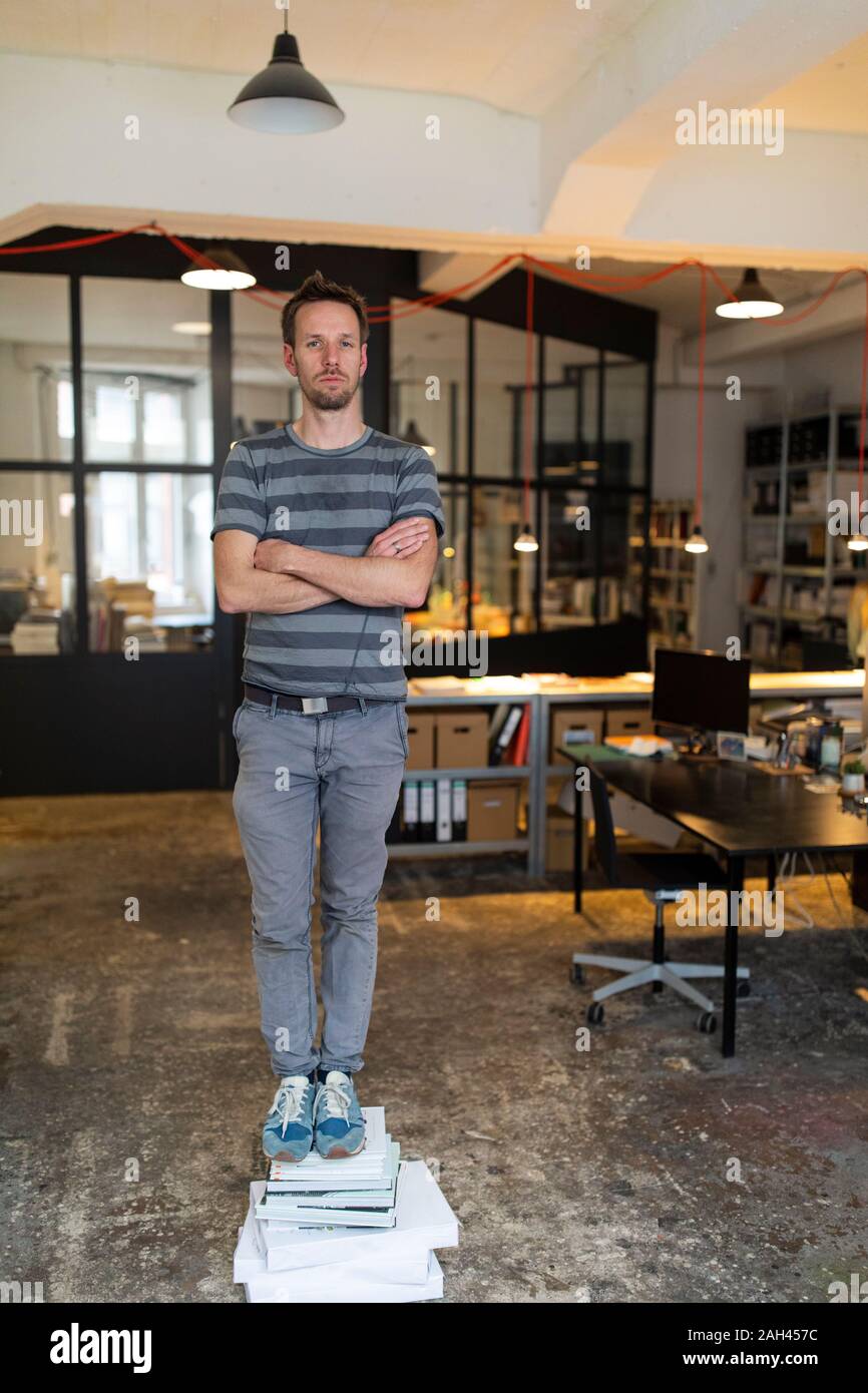 Casual man standing on stack of books in office Stock Photo - Alamy