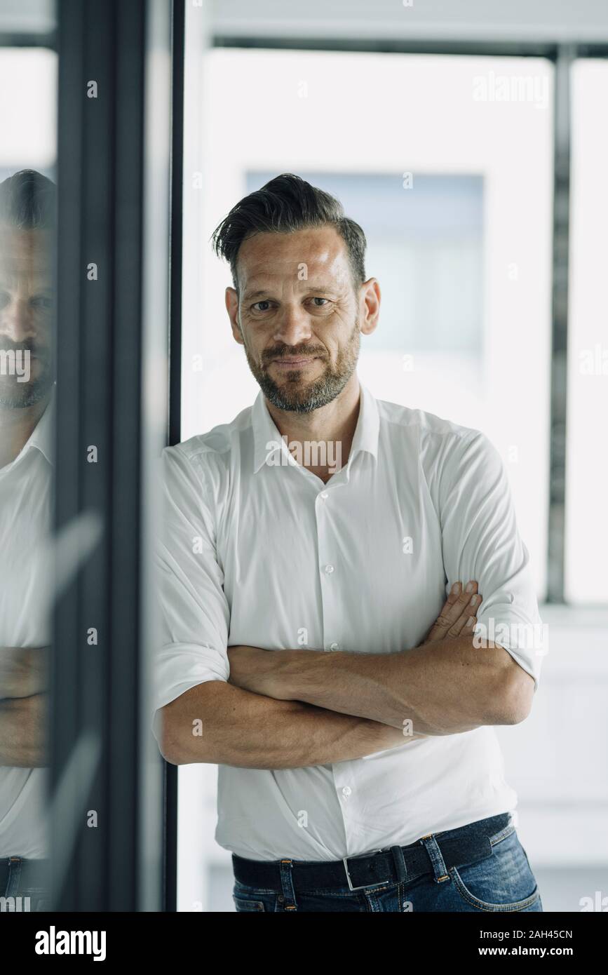 Confident businessman leaning against glass wall hi-res stock ...