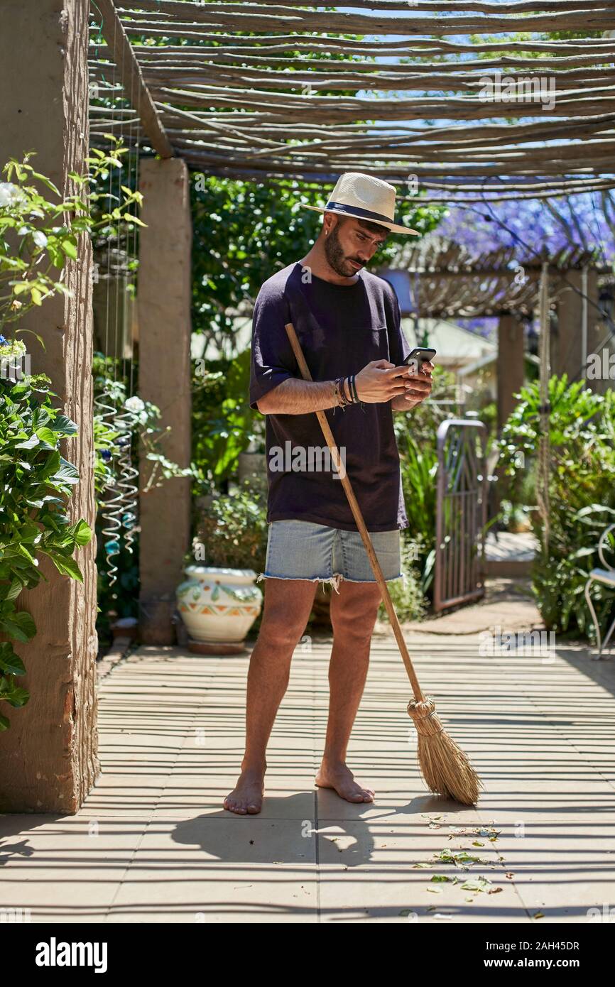 Man with broom using his smartphone outdoors Stock Photo - Alamy