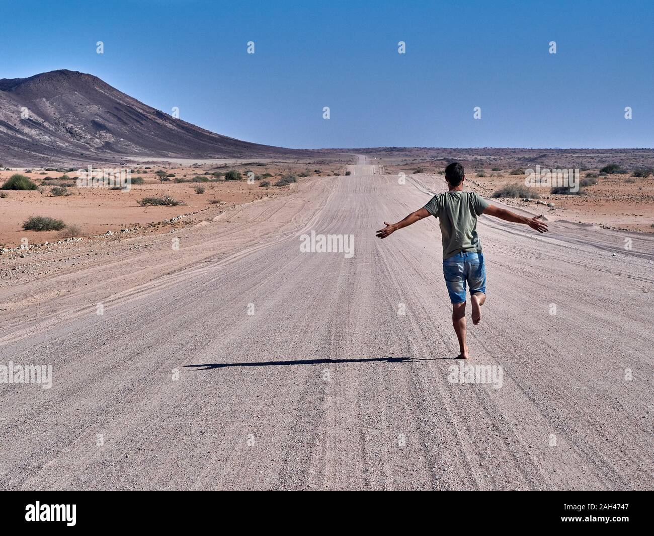 Man running freely on an endless road, rear view, Damaraland, Namibia ...