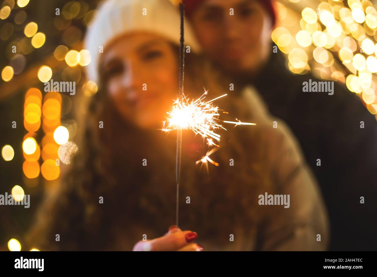 A sparkler burns in the hands of a girl hugged by her boyfriend in a ...