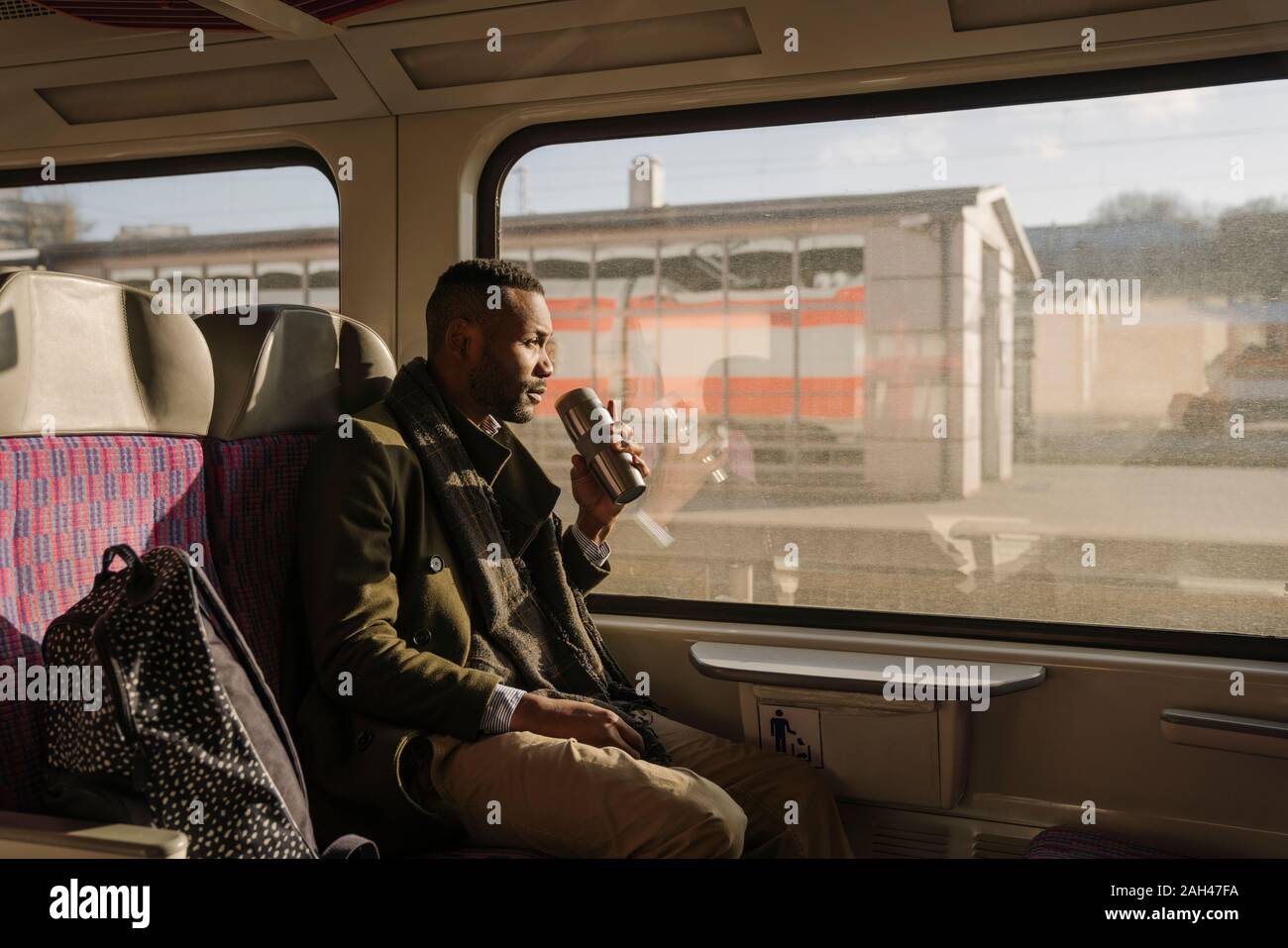 Stylish man drinking hot drink from reusable cup while traveling by ...