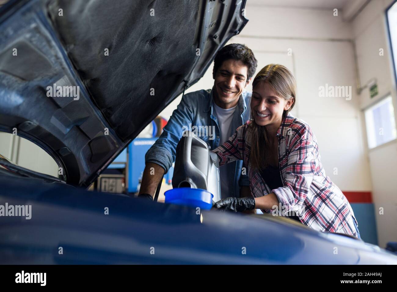 Young woman pouring lubricant in funnel while man standing near and ...