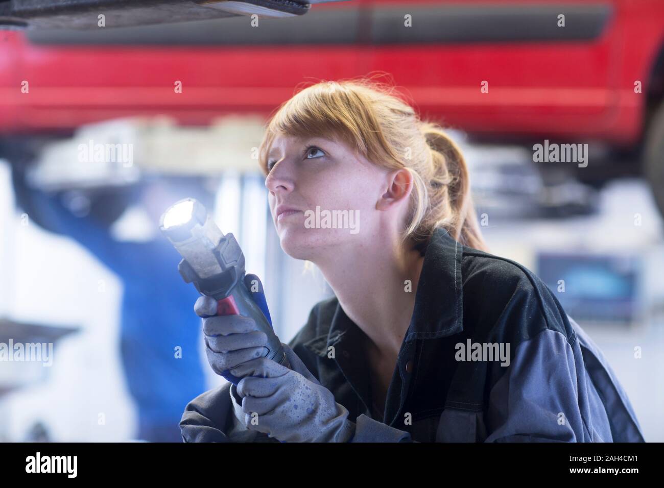 Female car mechanic with lamp looking to bottom of a car in repair ...