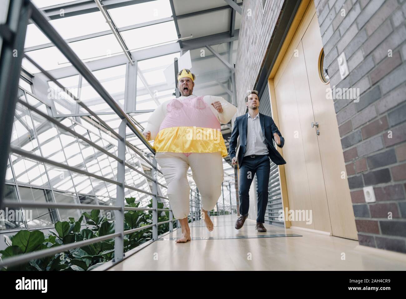 Businessman and man dressed up as a ballerina running in modern office ...