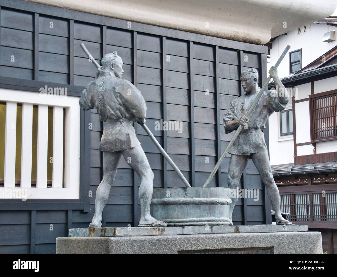 The statue of two traditional sake brewery workers stirring a container ...