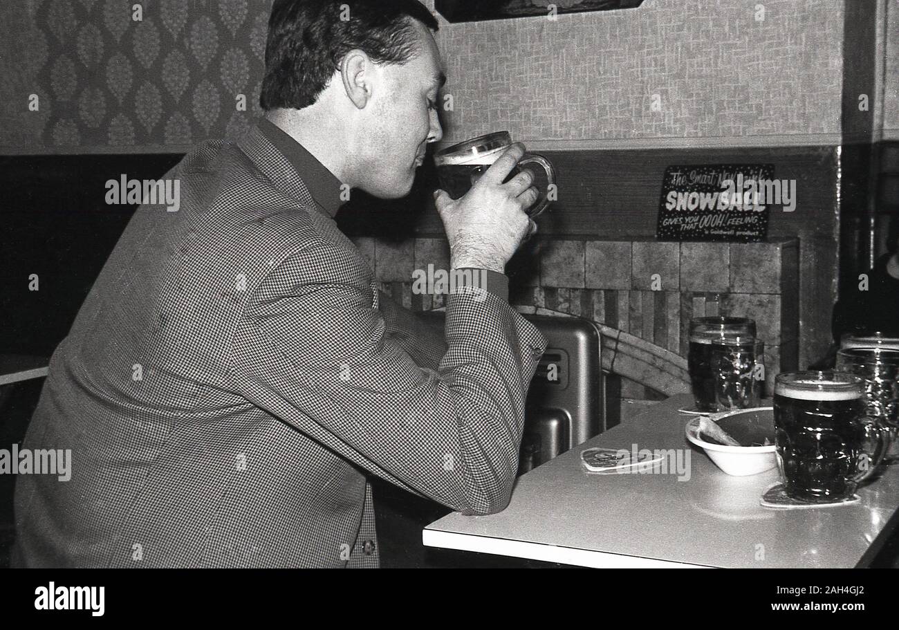1960s, historical, a man sitting at a table in a bar or pub drinking a ...