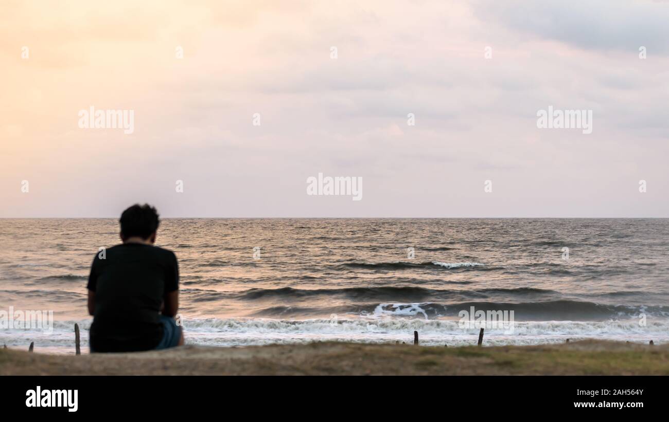 Blur image of a solitary man sitting alone at the beach in sunset time ...