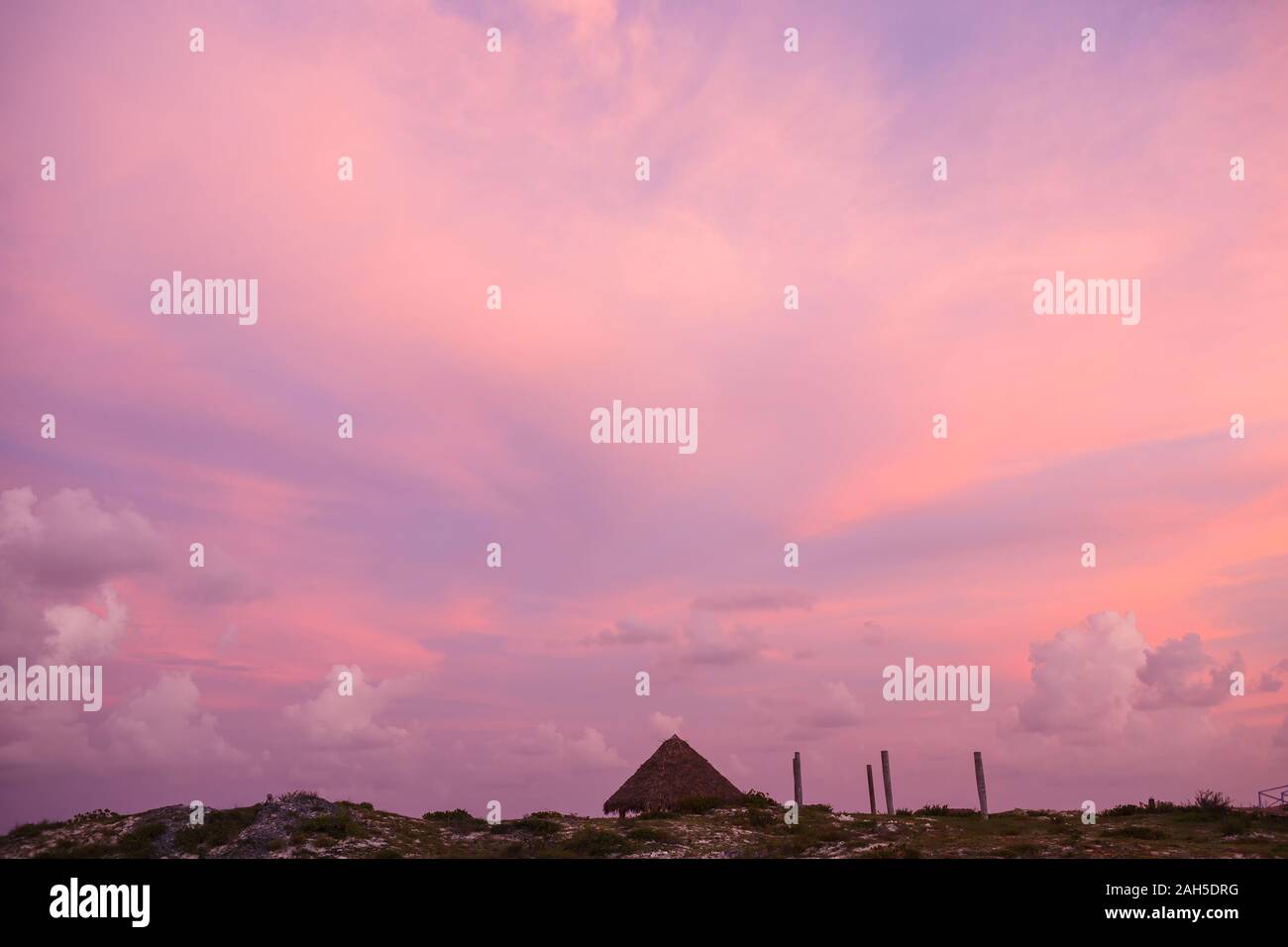 Amazing sunset on sea shore. Domed thatched roof is seen against pastel ...