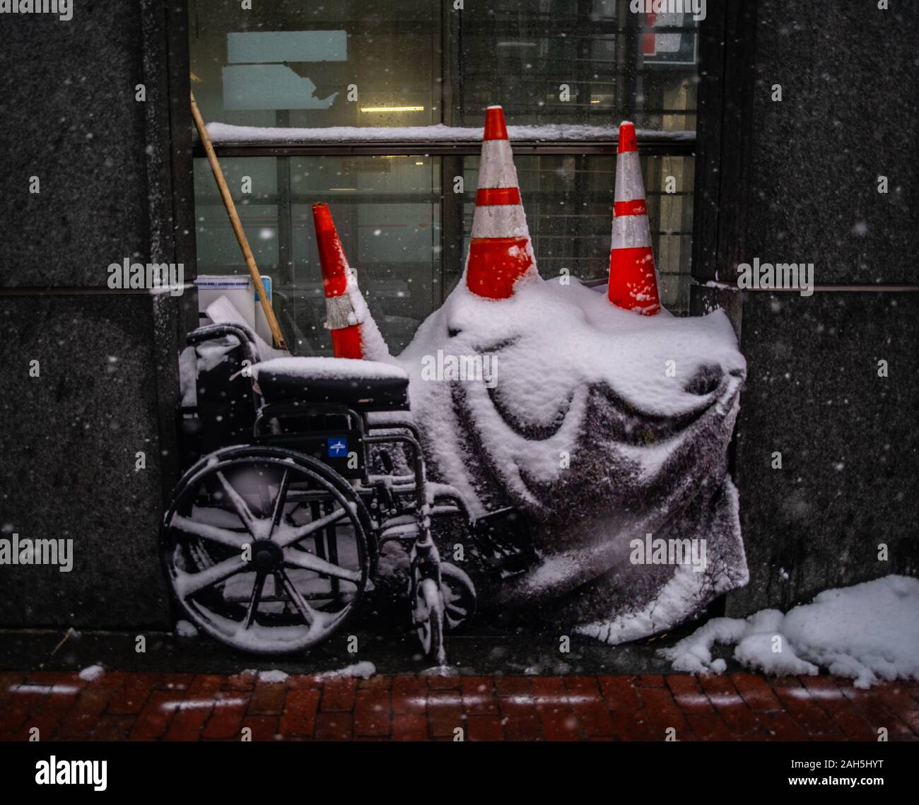 Snow piles up on a wheelchair and a tarp covering something and held ...