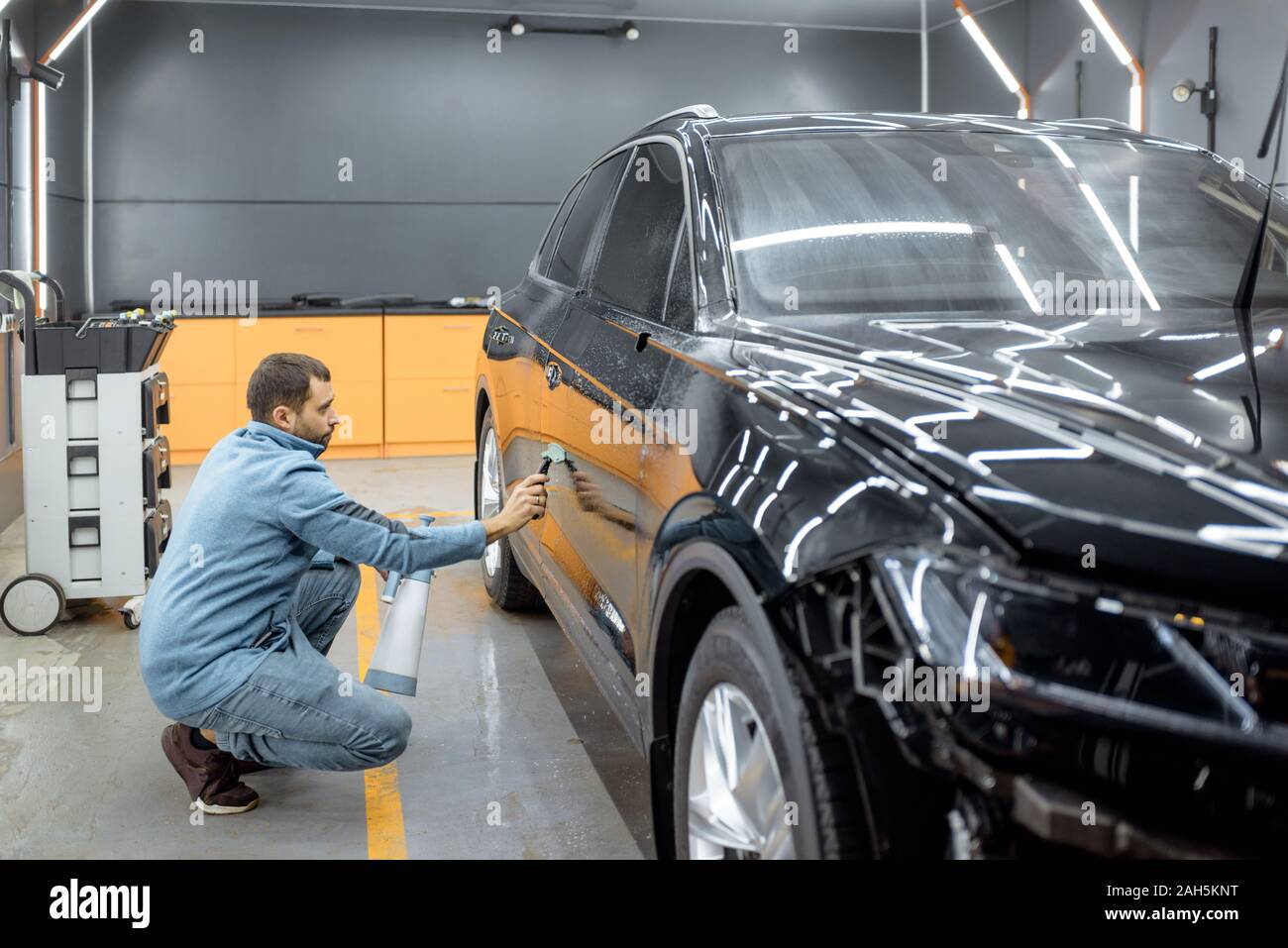 Car service worker removing water from the car body with a scraper ...