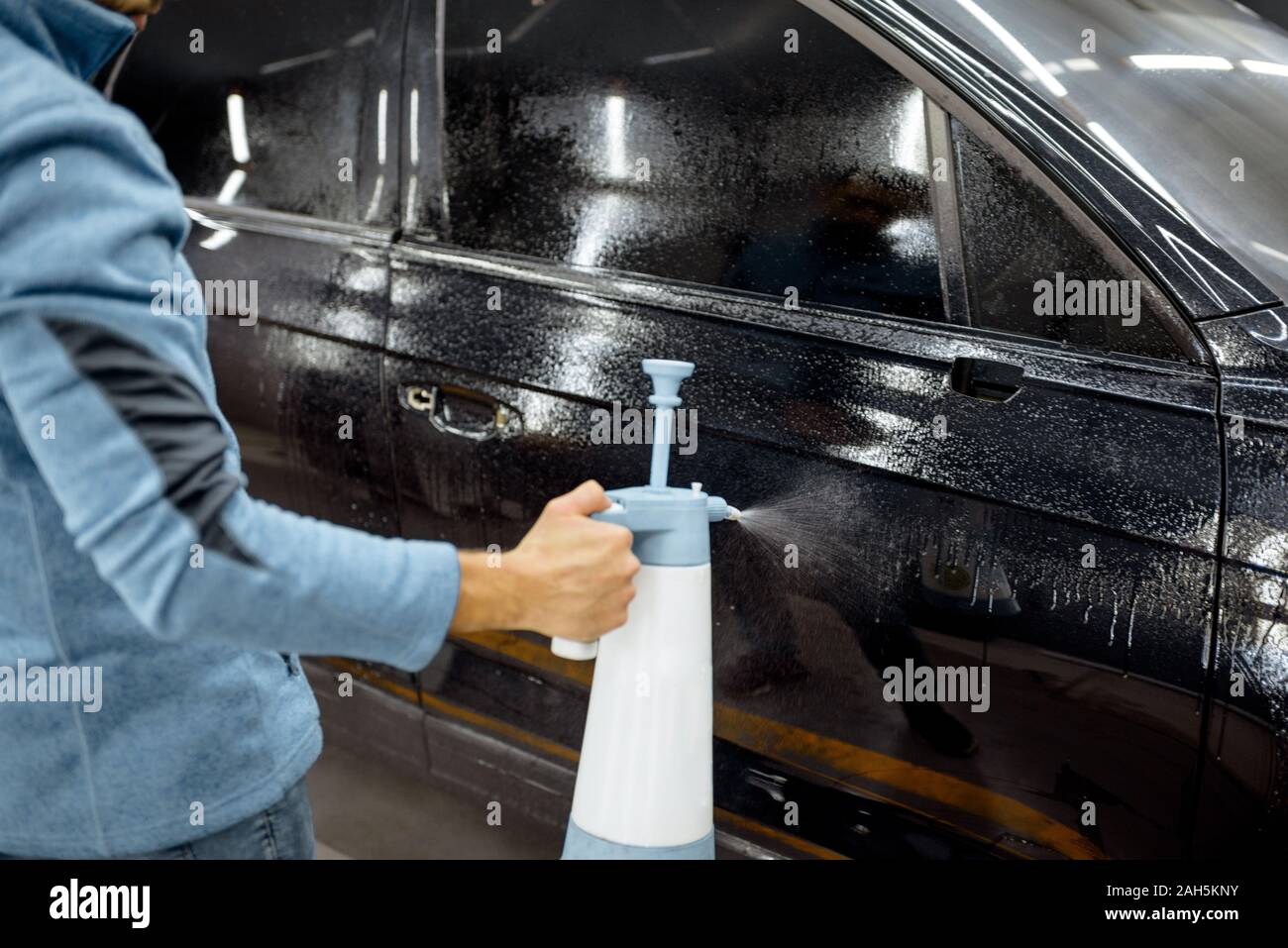Car service worker splashing water on the car body, wetting it before ...