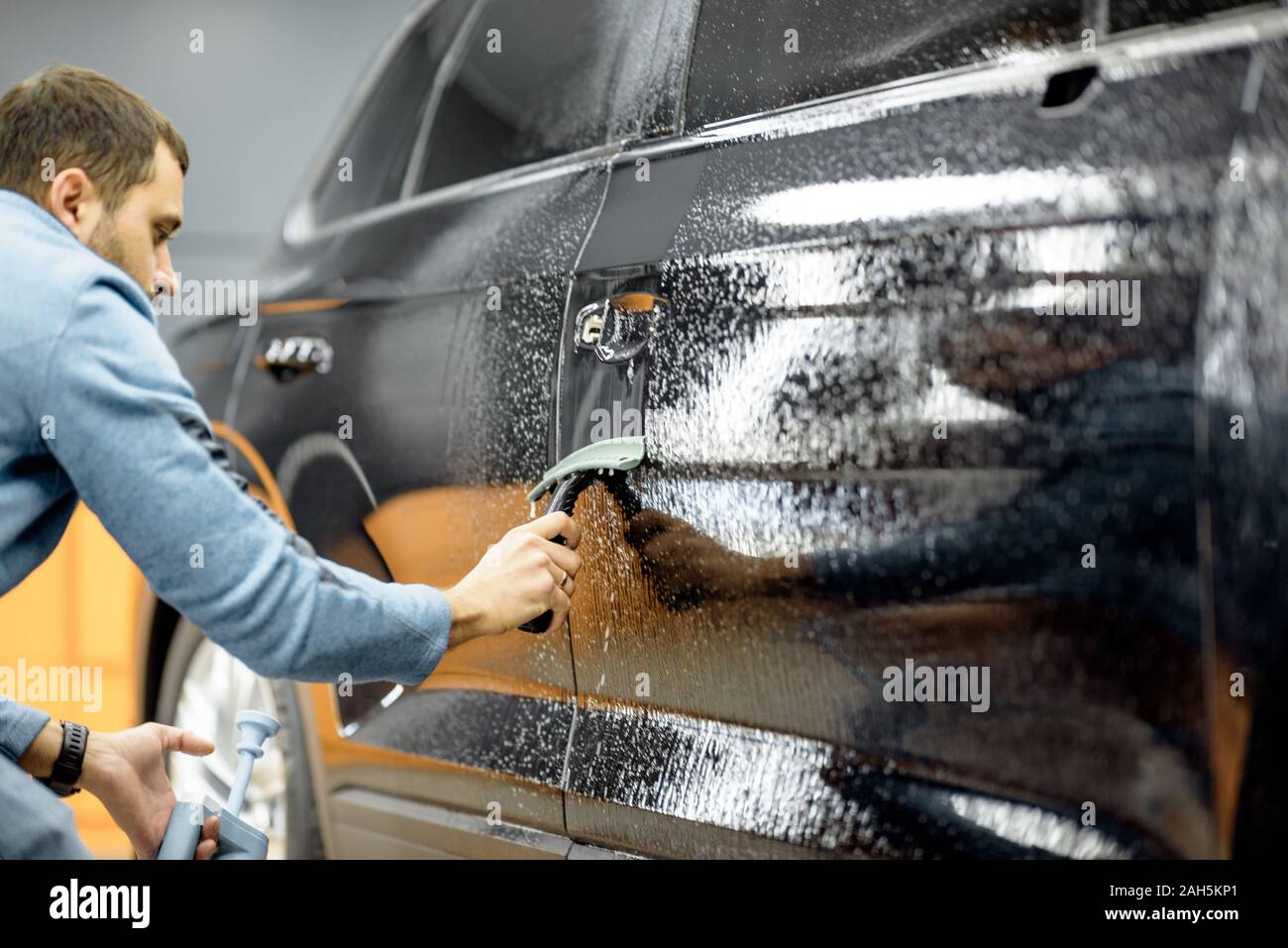 Car service worker removing water from the car body with a scraper ...