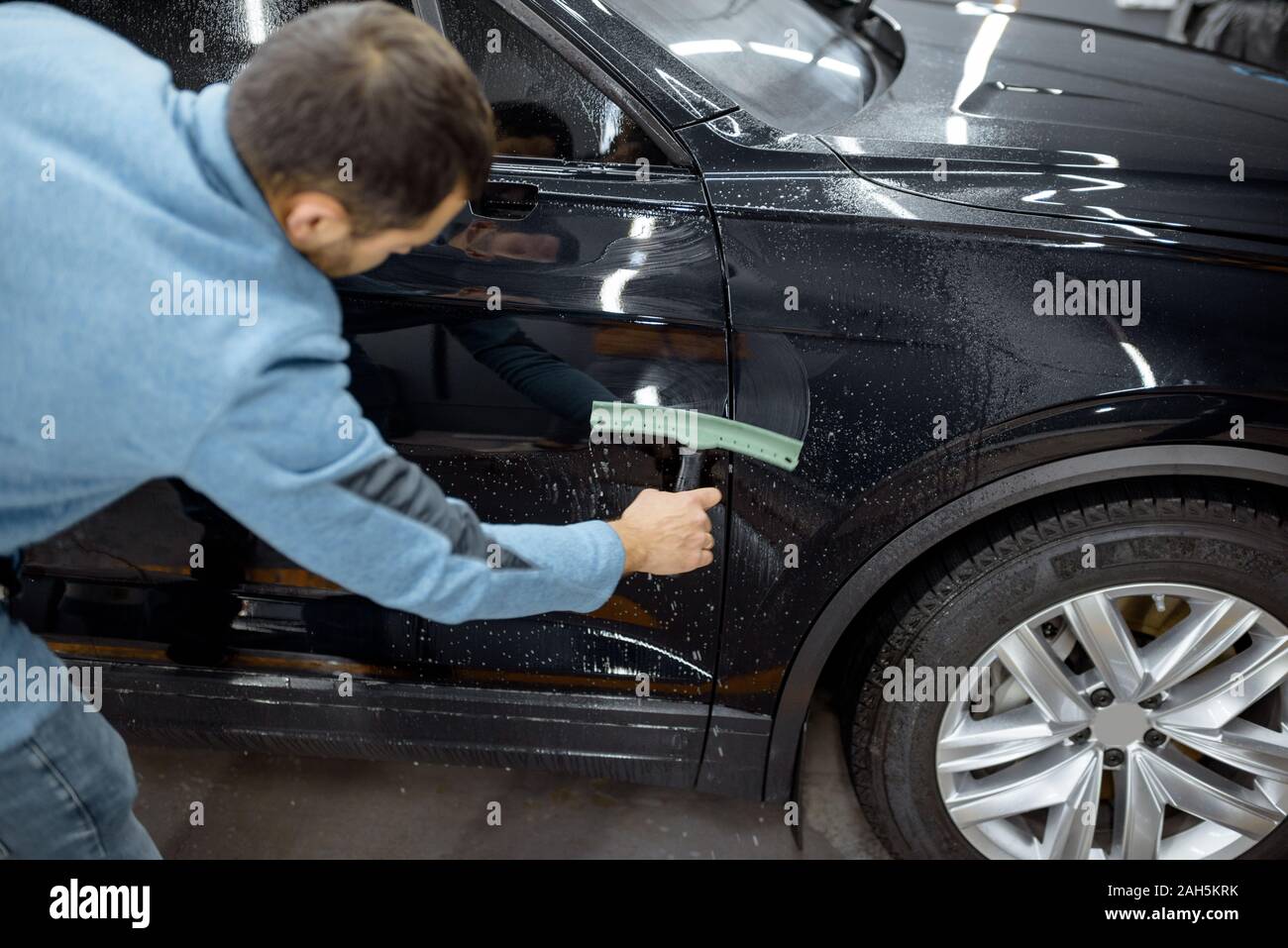Car service worker removing water from the car body with a scraper ...