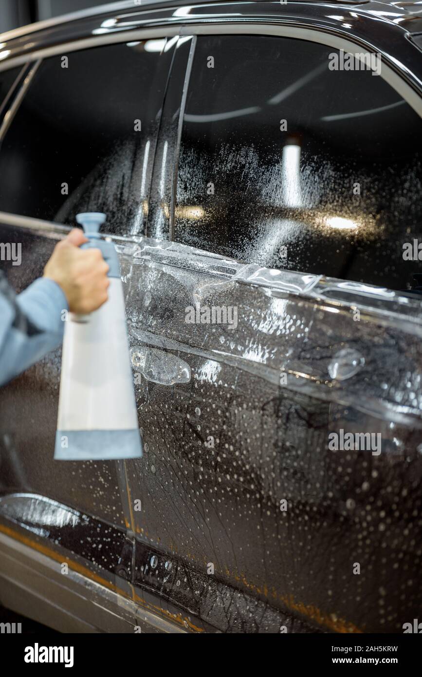 Car service worker splashing water on the car body, wetting it before ...