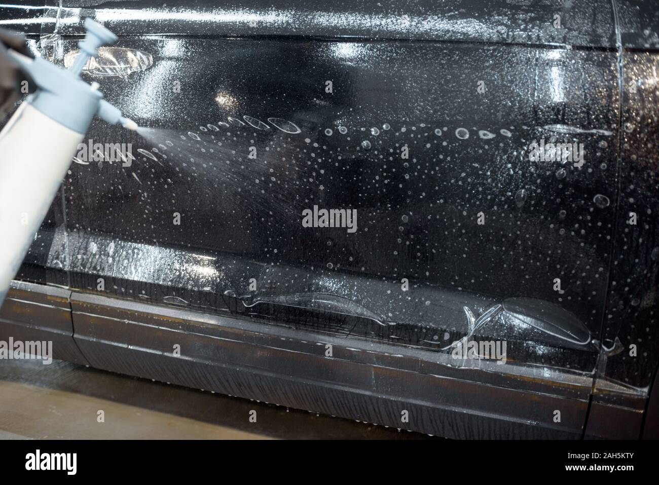 Car service worker splashing water on the car body, wetting it before ...