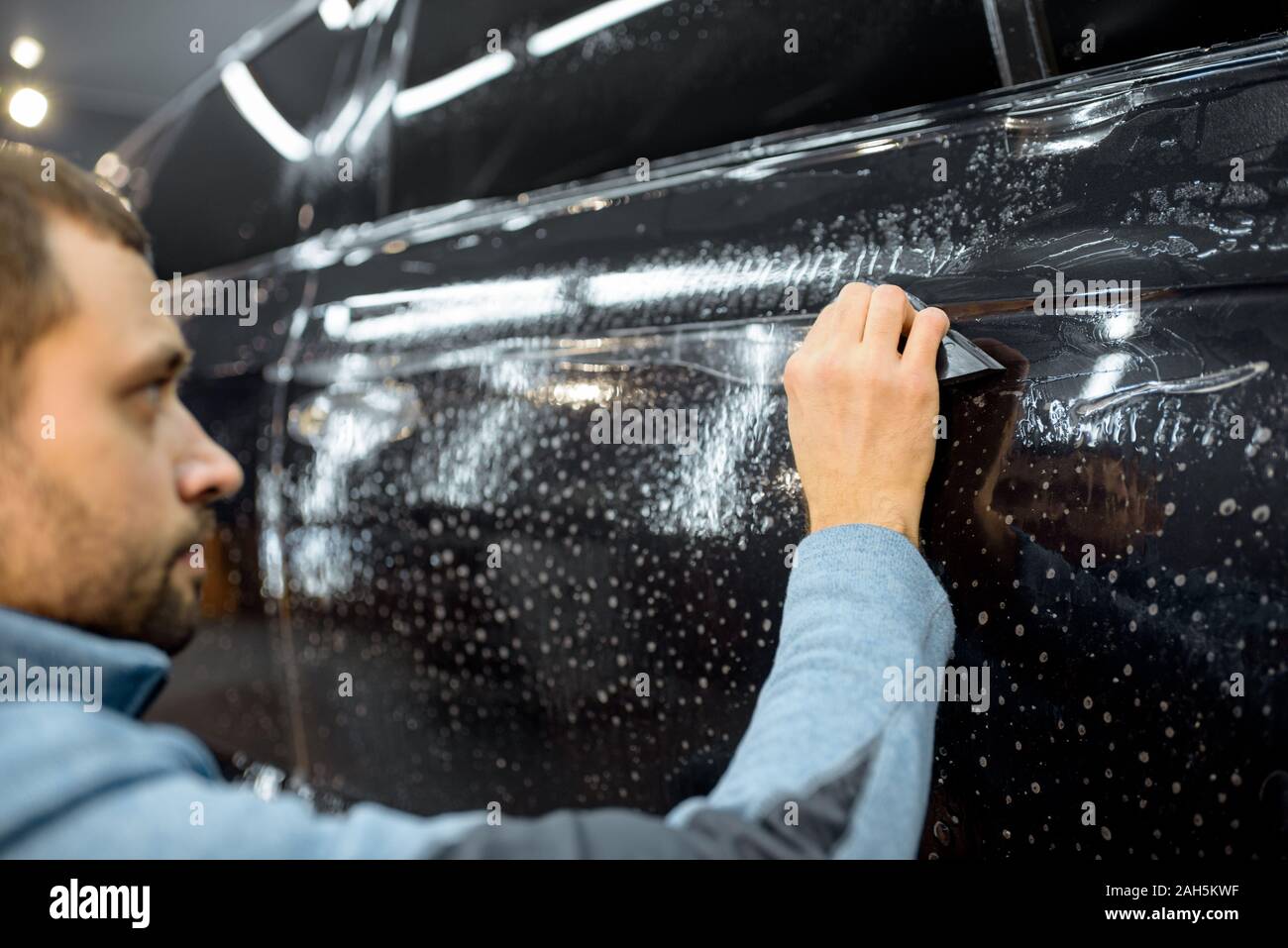 Car service worker sticking anti-gravel film on a car body with ...