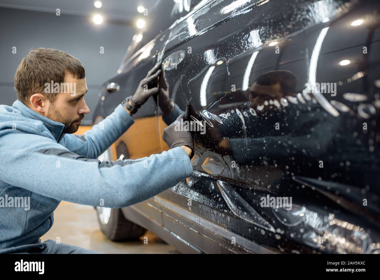 Car service worker sticking anti-gravel film on a car body with ...