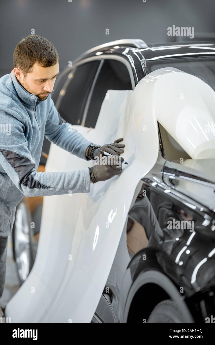 Man preparing protective film for sticking on a car body, marking it to ...