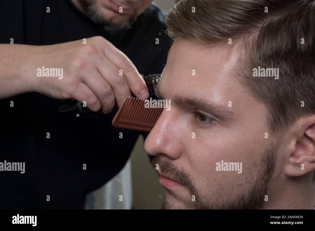Hairdresser cuts hair with a trimmer for a young guy with a beard ...