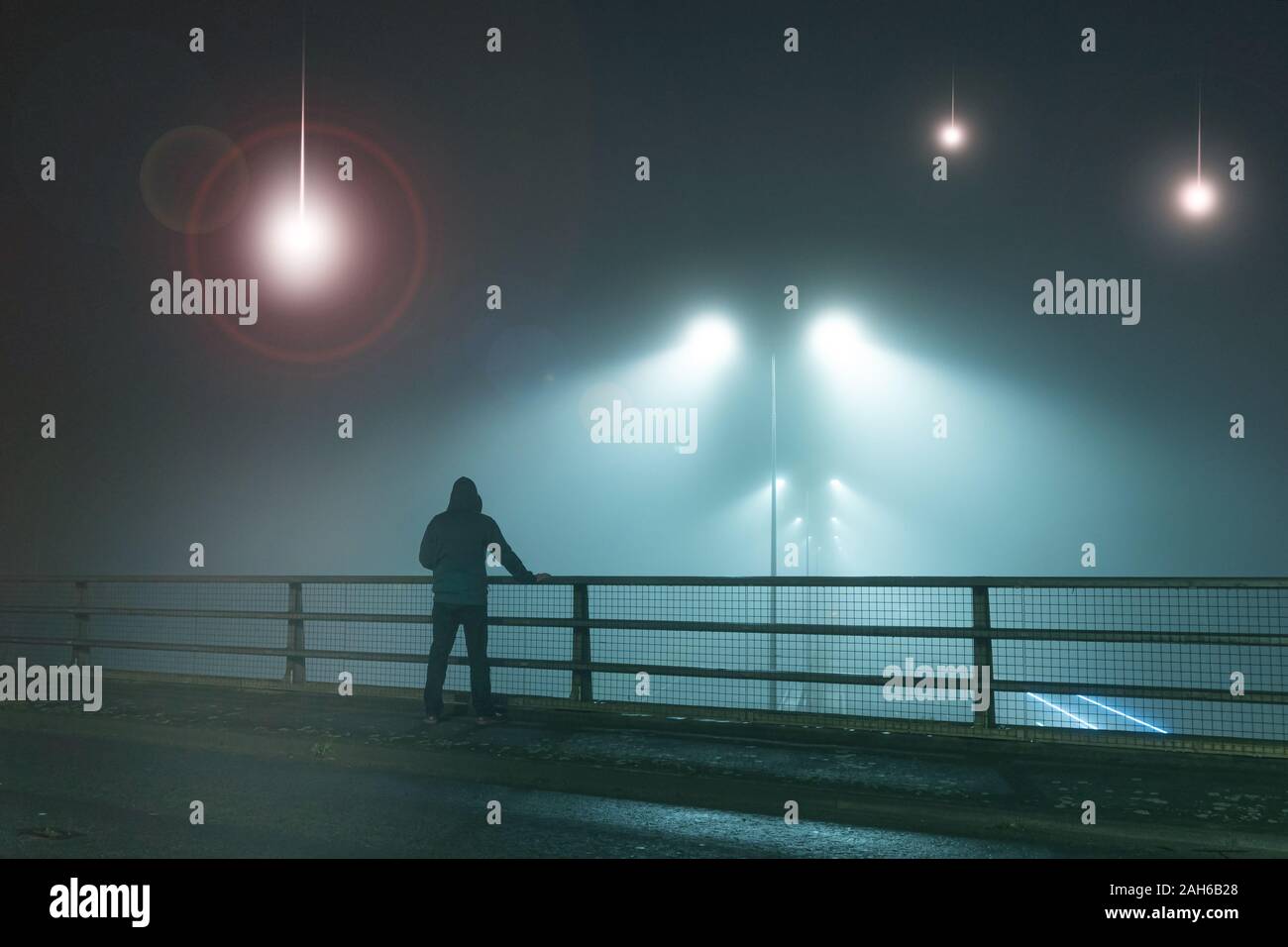 A hooded figure, standing with back to camera on a bridge, looking at ...