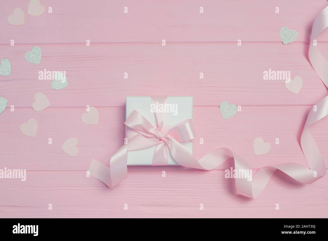 Gift box with ribbon and confetti in form of heart on pink wooden ...