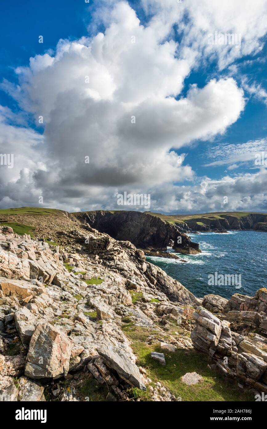 Scottish landscape with a rocky coastline under a blue sky with puffy ...