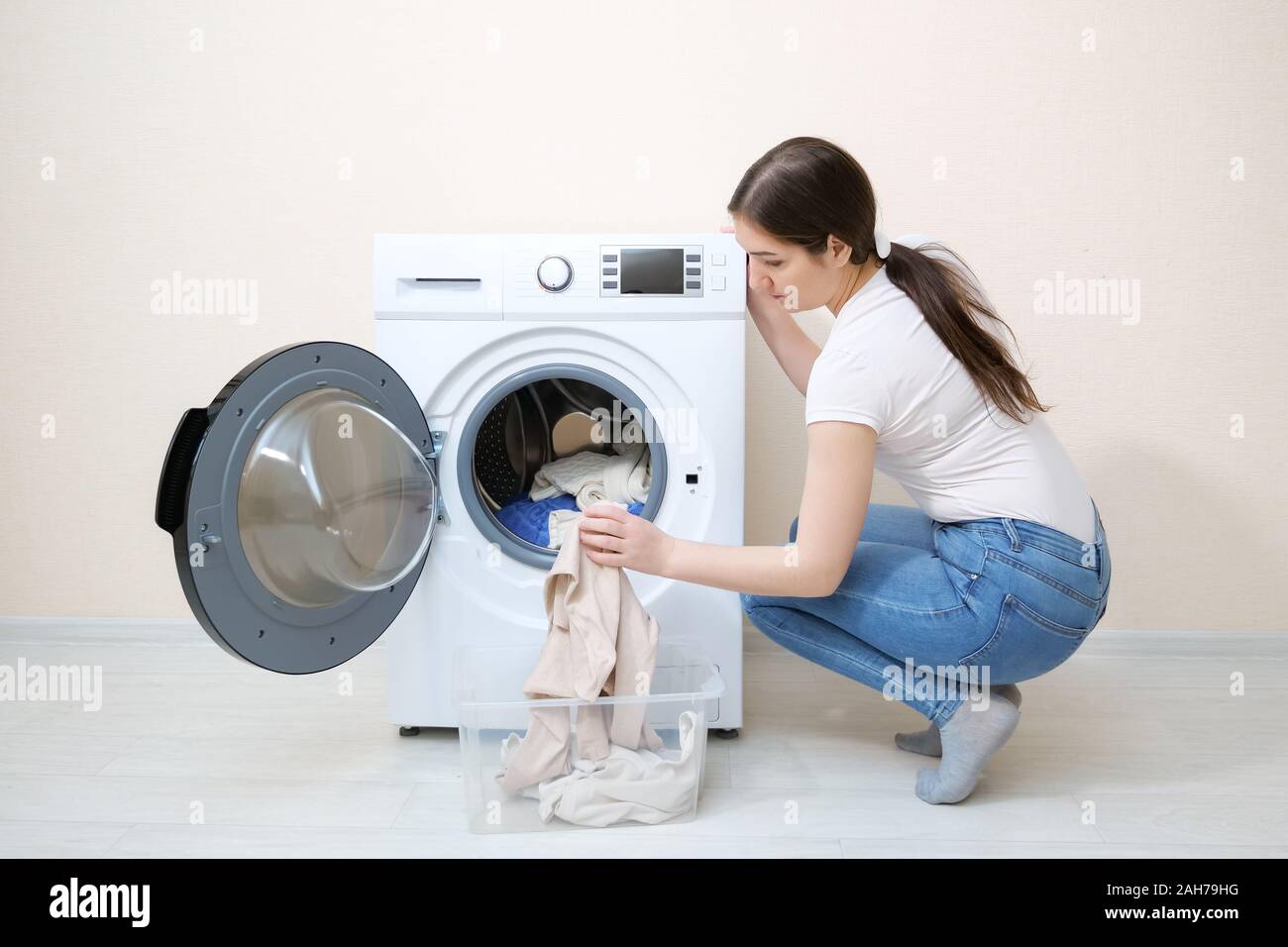 young brunette woman loads dirty clothes into modern washing machine ...