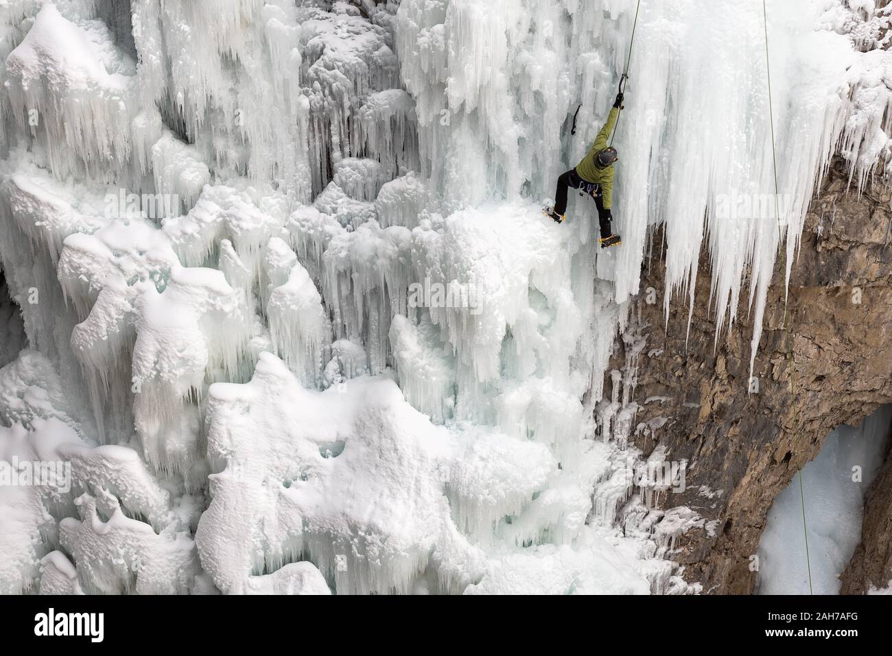 A solo male ice climber uses climbing equipment to work his way up ...