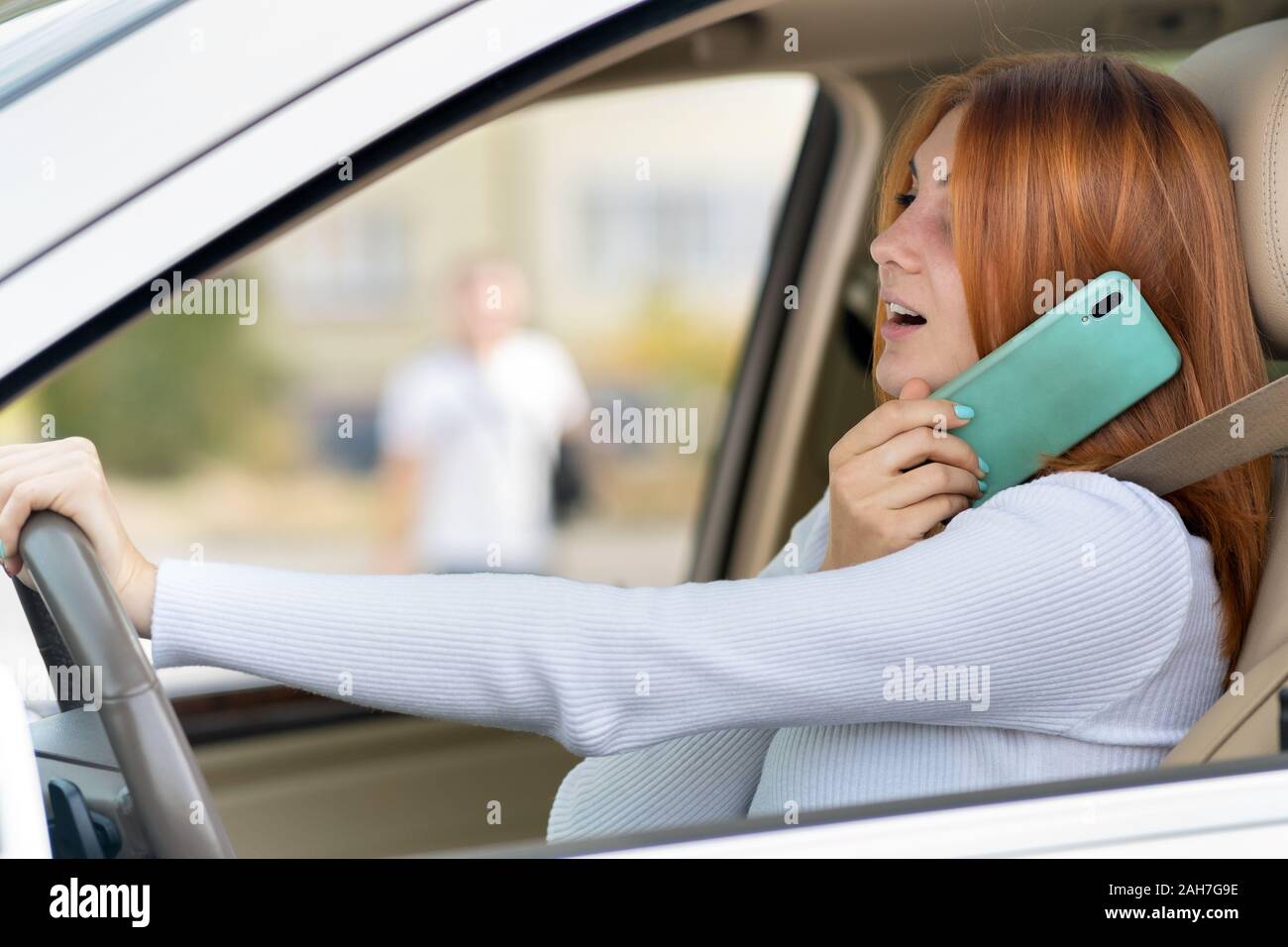Happy redhead girl talking on her mobile phone behind the wheel driving ...