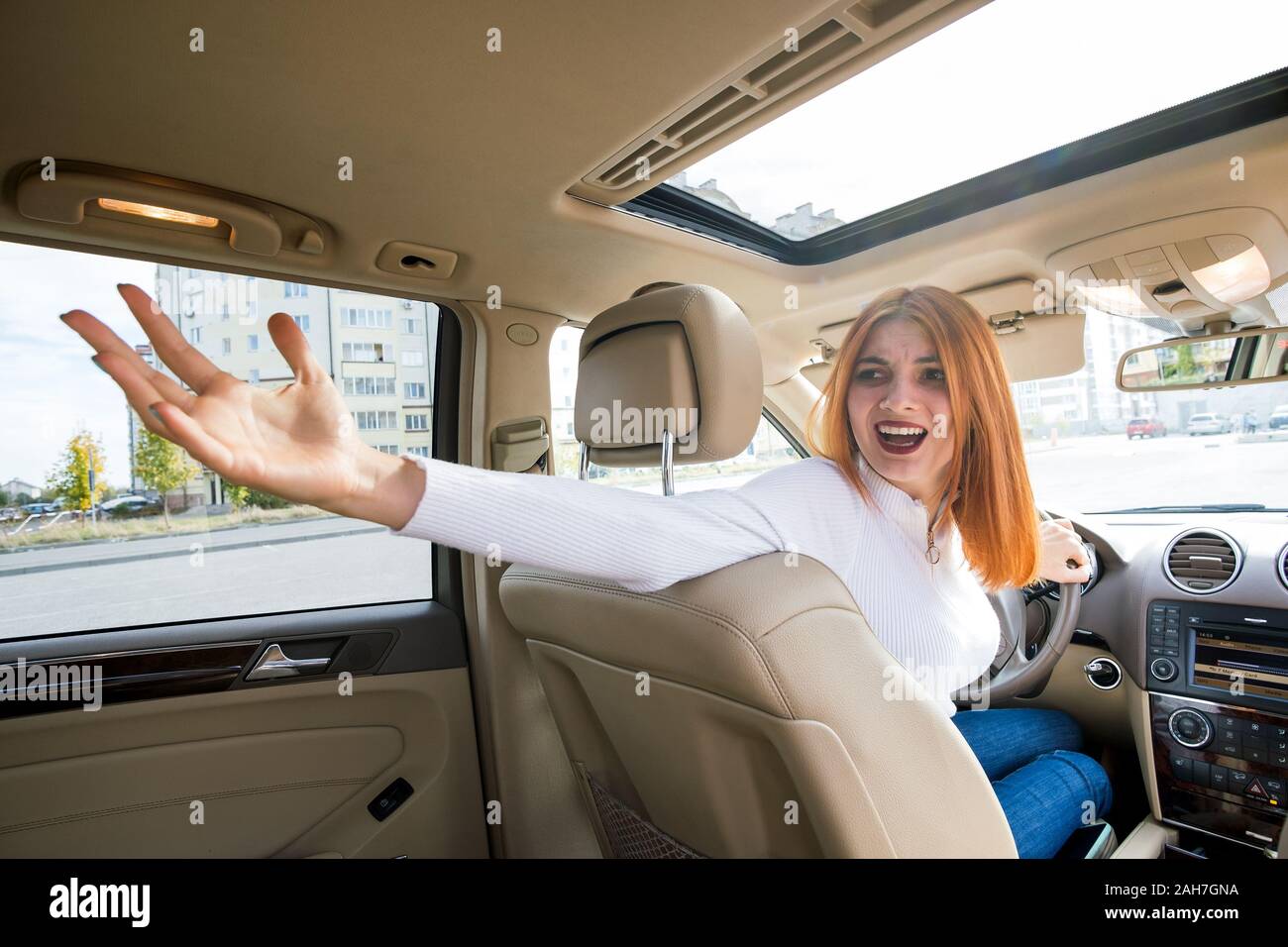 Wide angle view of young redhead woman driver driving a car backwards ...