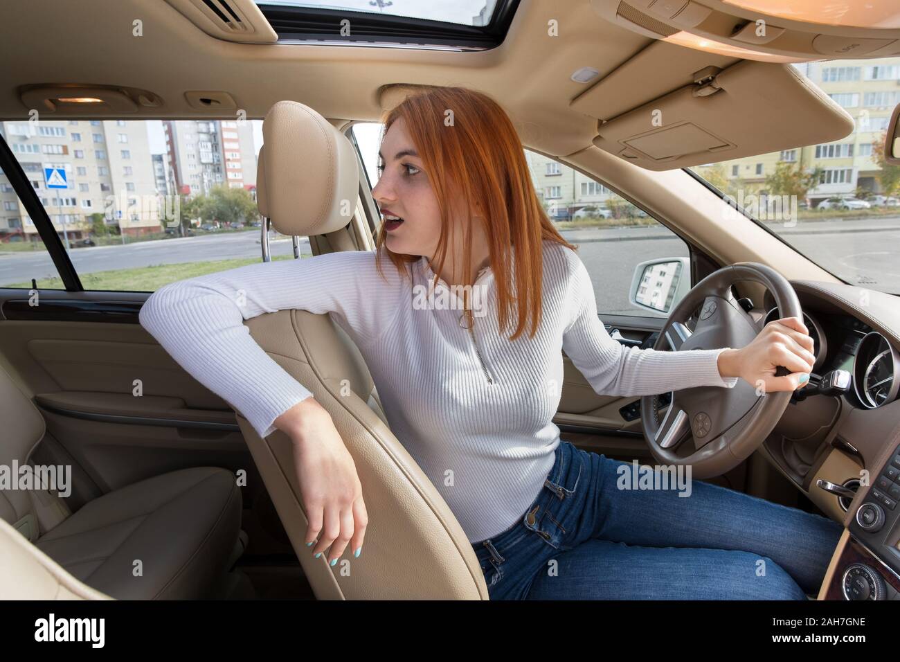Wide angle view of young redhead woman driver driving a car backwards ...