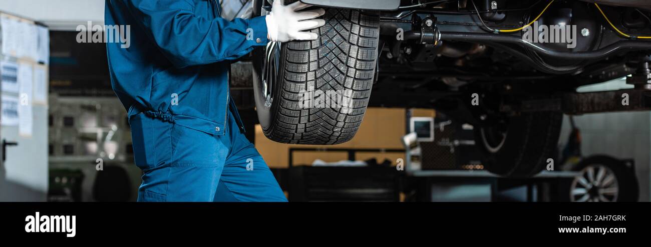 cropped view of mechanic installing wheel on car in workshop, panoramic ...