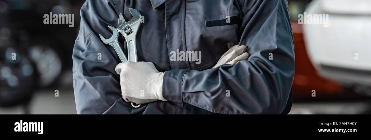 cropped view of mechanic holding wrenches while standing with crossed ...