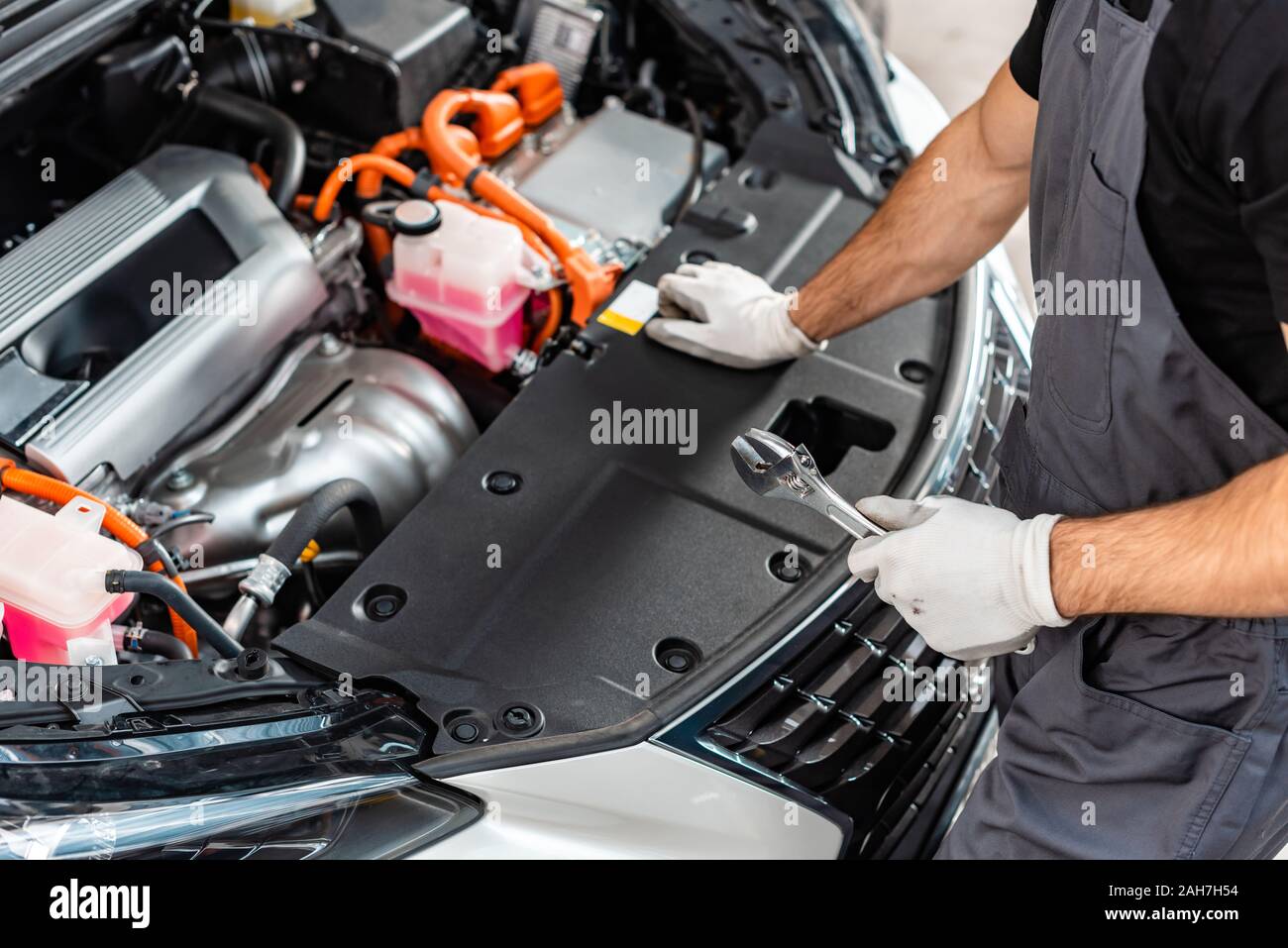 partial view of mechanic holding wrench while inspecting car engine ...