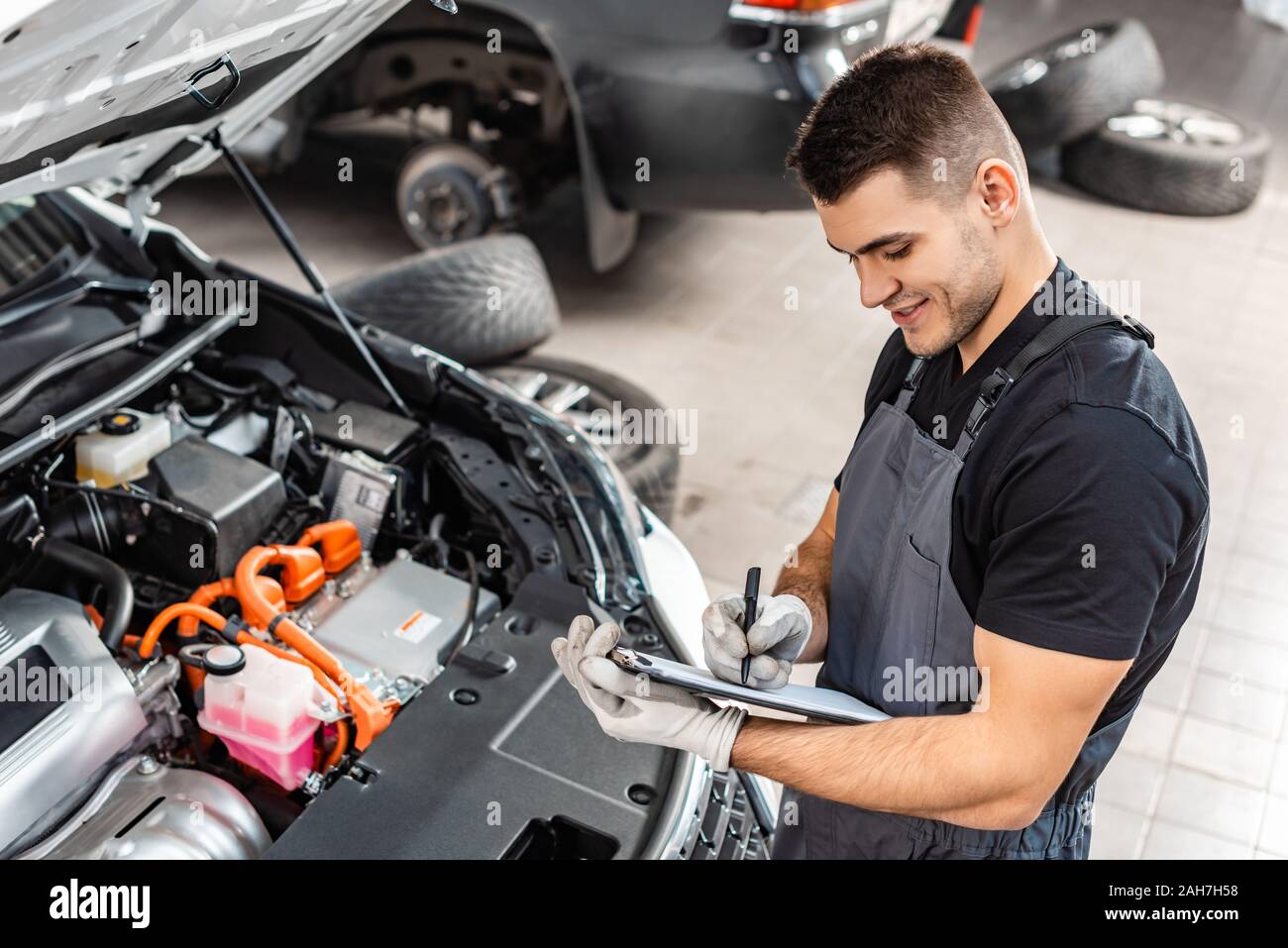 smiling mechanic writing on clipboard while inspecting car engine ...