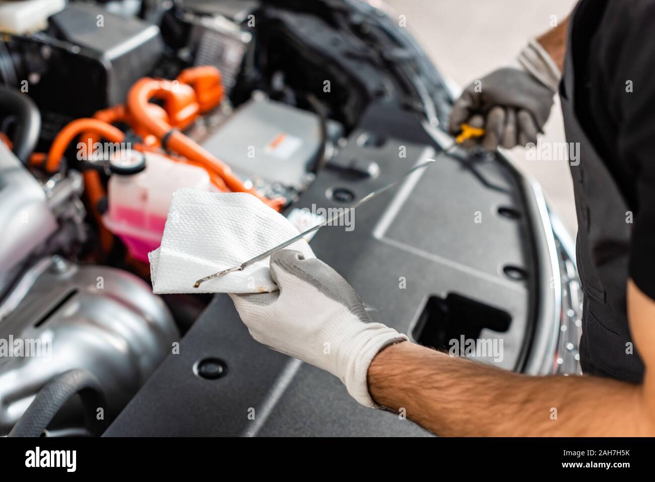 cropped view of mechanic wiping oil dipstick with rag near car engine ...