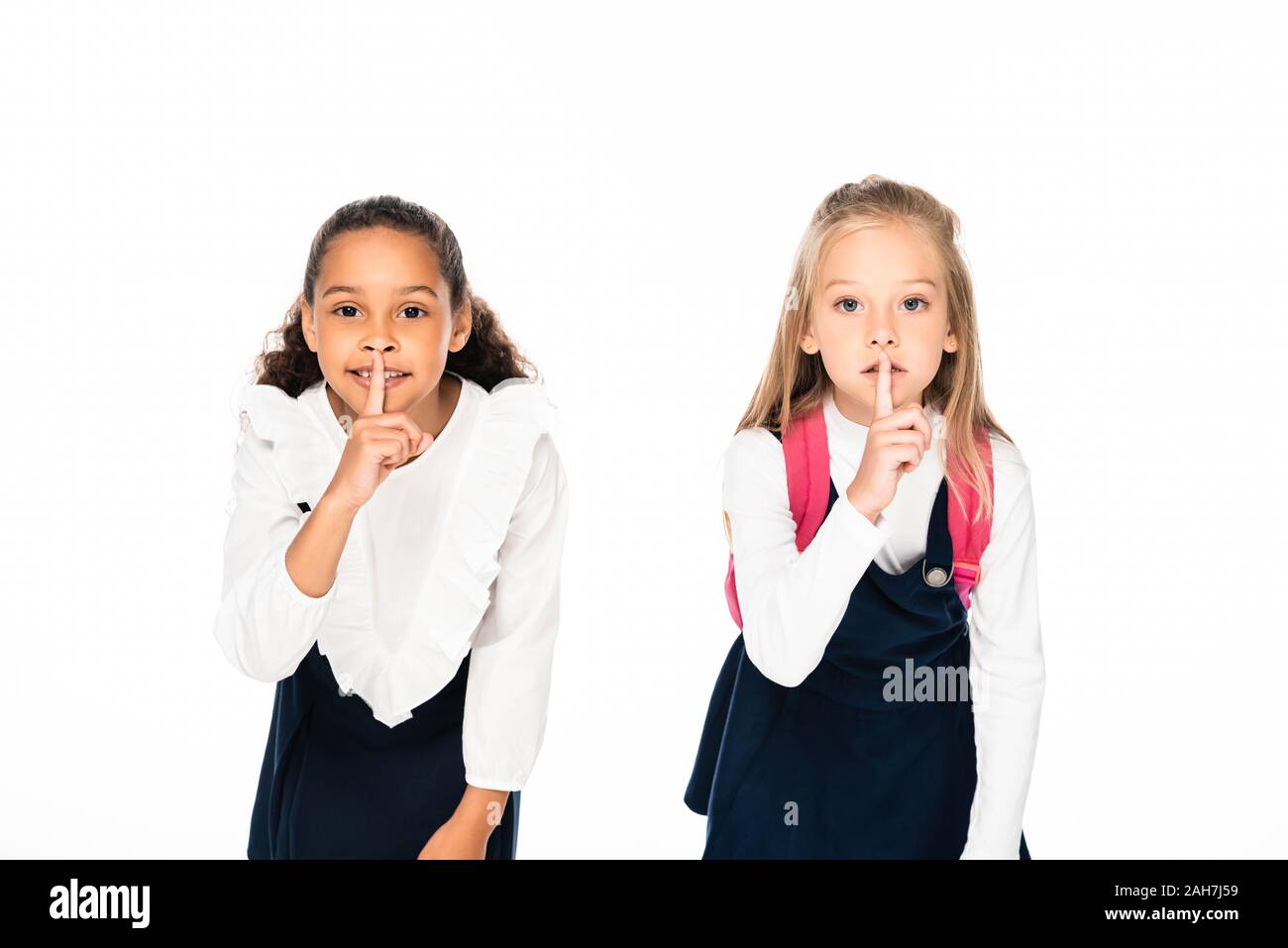 two adorable multicultural schoolgirls showing hush gestures isolated ...