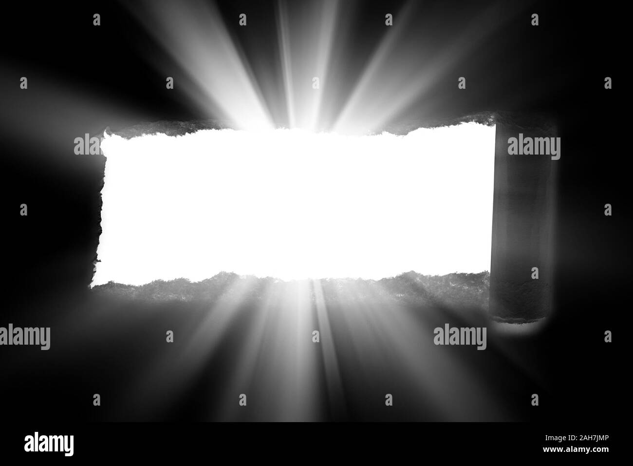 A hole in black paper with torn edges and piercing sunlight and rays ...