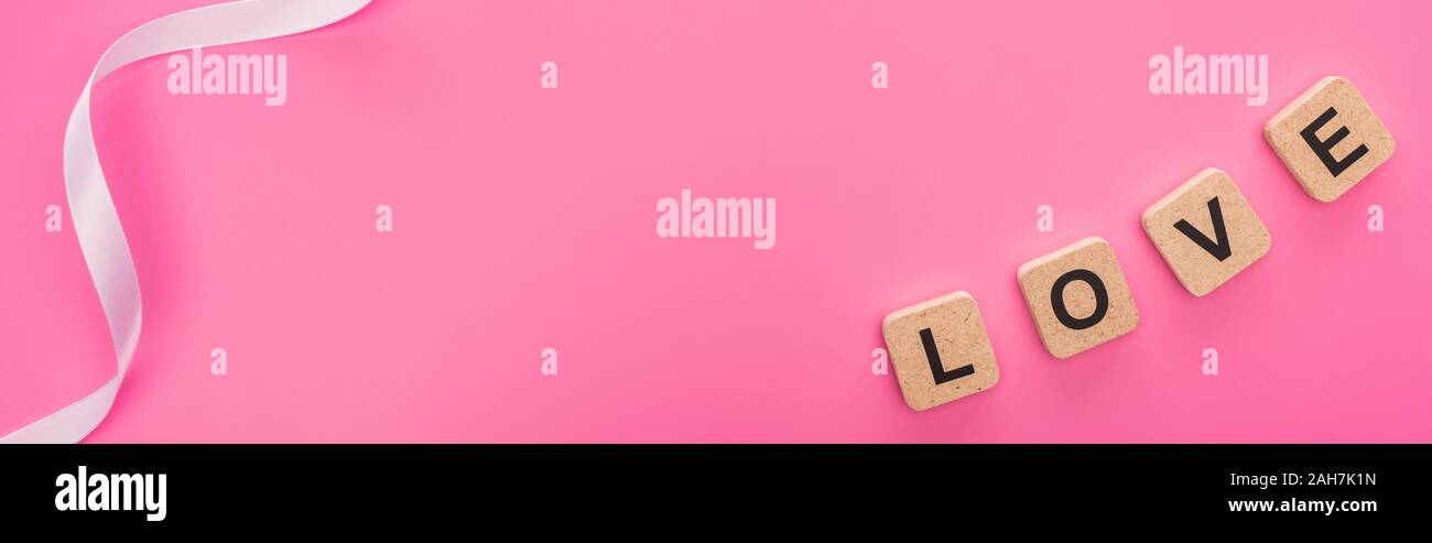 top view of ribbon and love lettering on wooden cubes isolated on pink ...