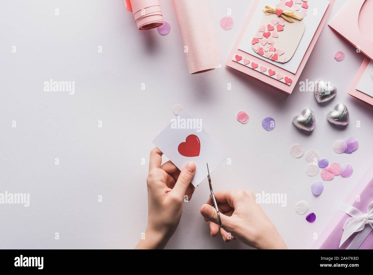 cropped view of woman cutting out heart with scissors near valentines ...