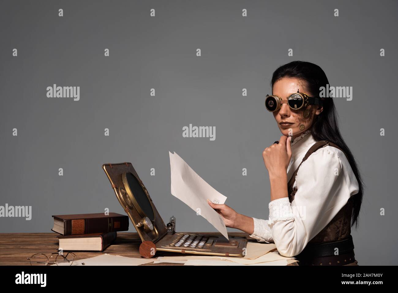 steampunk woman holding documents at table with vintage laptop isolated ...