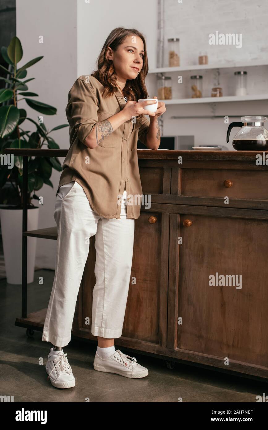 Young woman with prosthetic leg drinking coffee by kitchen table Stock ...