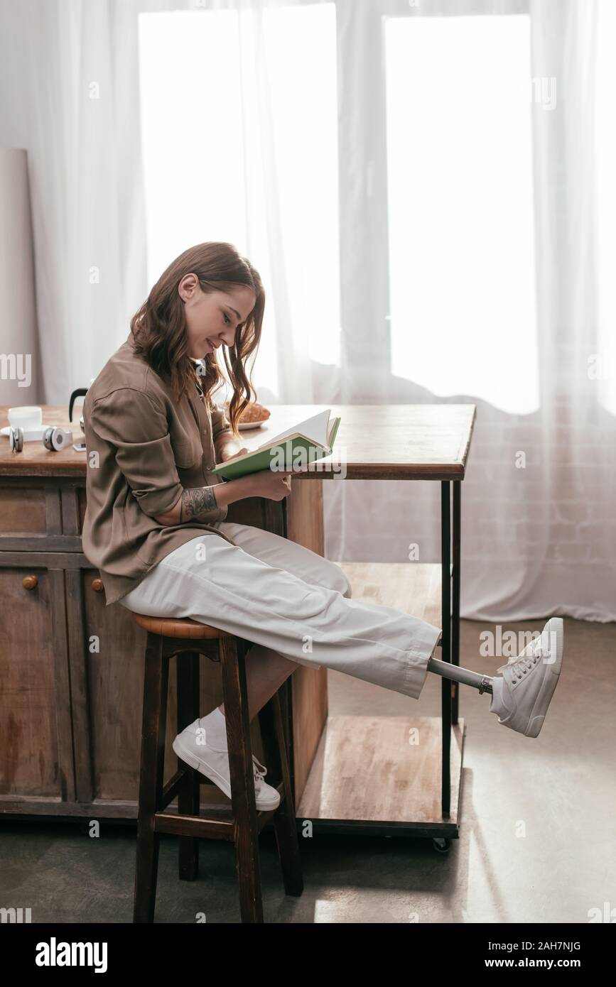Side view of smiling woman with leg prosthesis reading book beside ...