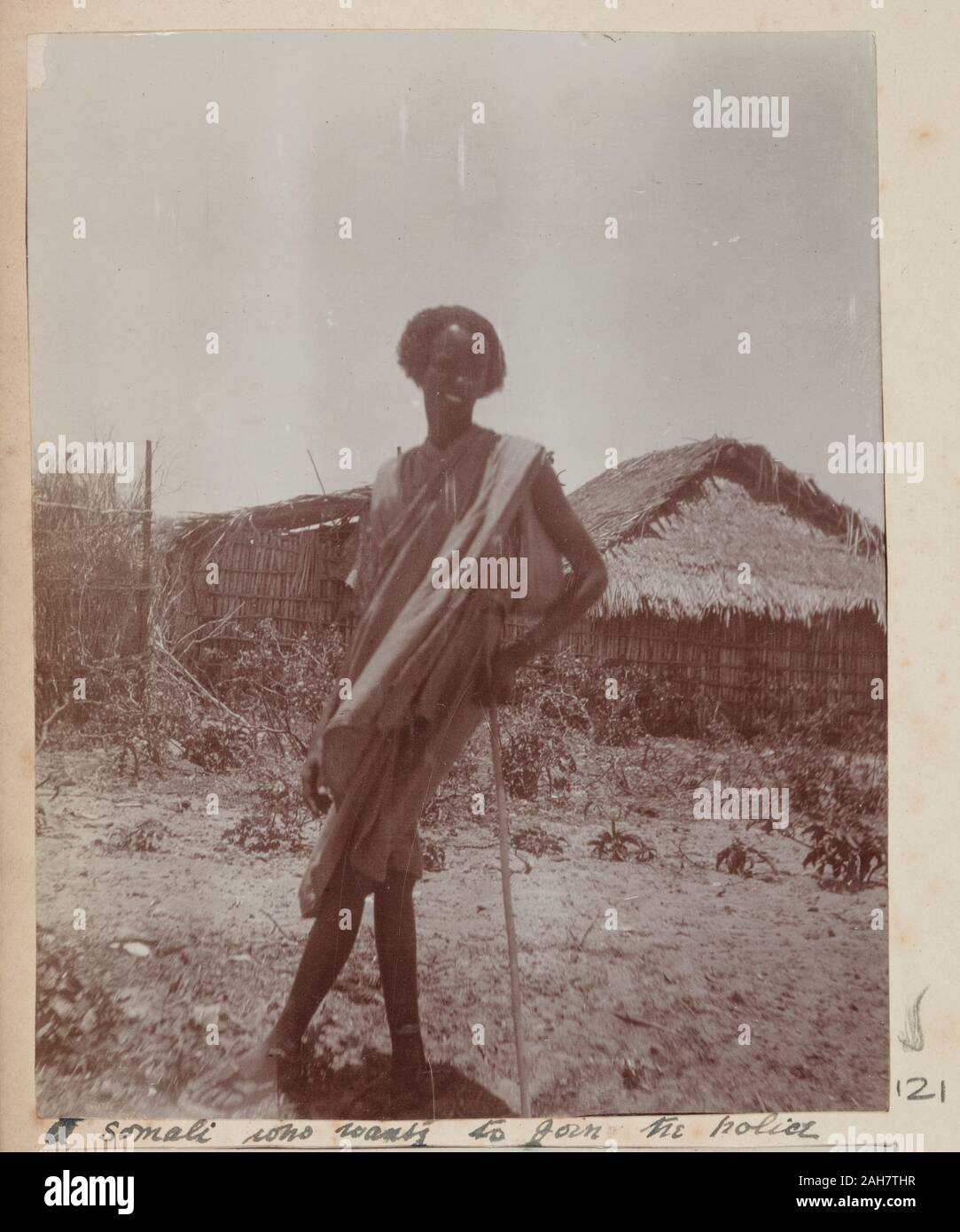 SomaliaJubaland, Somali man leaning on a stick with grass hut behind ...