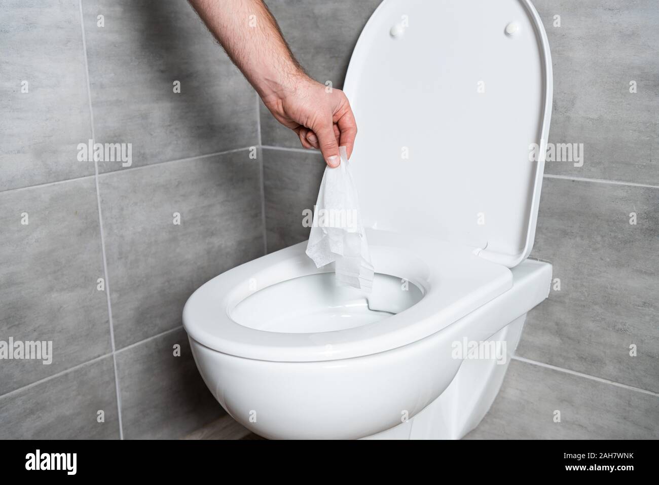 Cropped view of man throwing napkin in toilet bowl in bathroom with ...